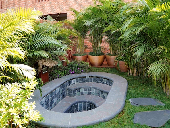 Um jardim com hidromassagem, plantas em vasos e um muro de tijolos.