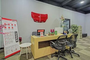 Uma receção com um computador, um telefone e uma pequena planta. Há um cartaz na parede e uma cadeira em frente à mesa.