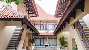 Um pátio com escadaria central, telhado em azulejos e um edifício com varandas.
