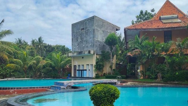 Piscina com jardim ao redor e um edifício com telhado de telhas vermelhas.