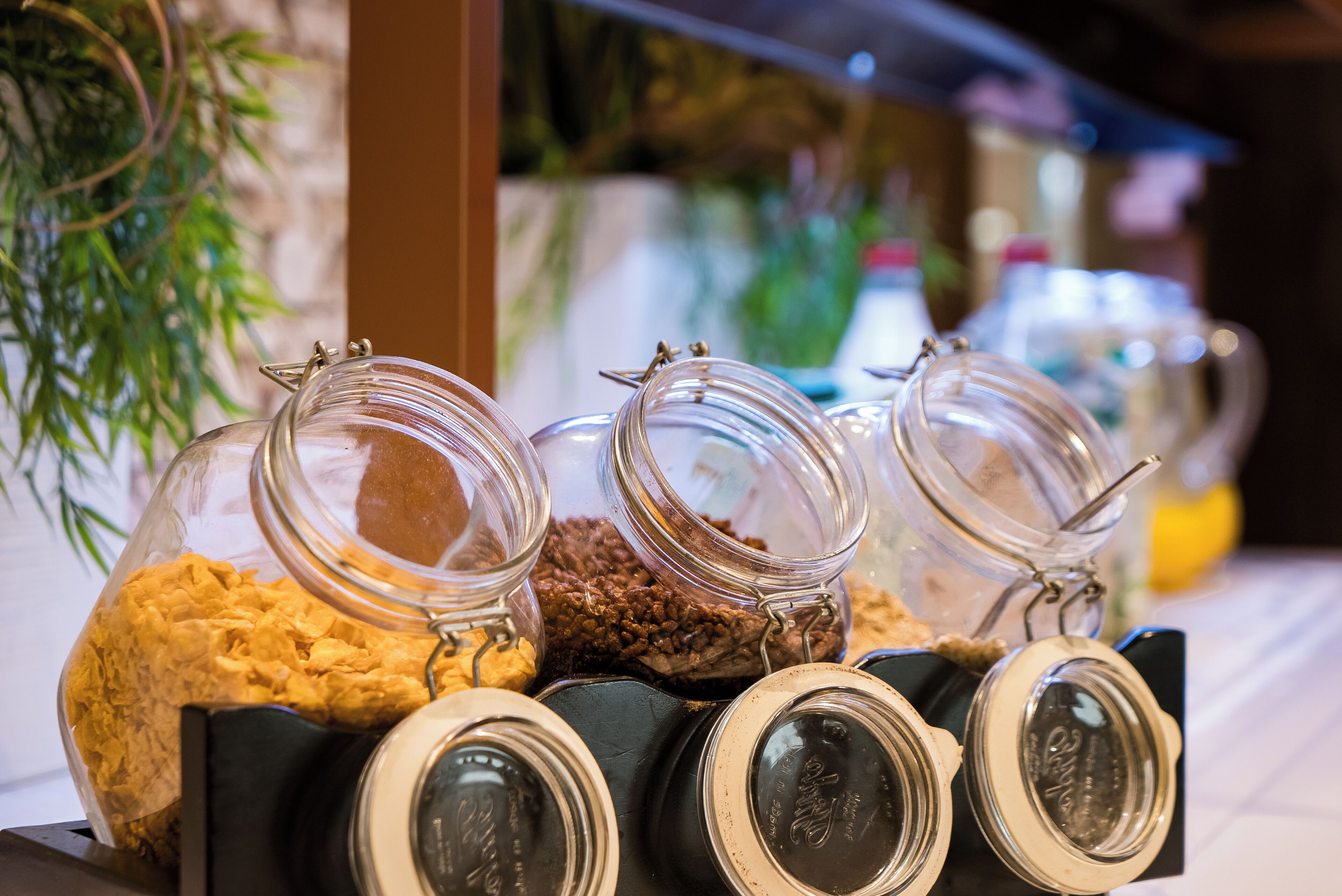Três potes de vidro com tampas de metal, contendo diferentes alimentos, colocados sobre um suporte preto.