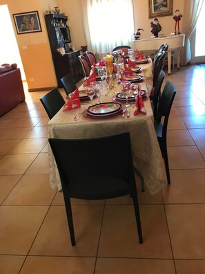 Uma sala de jantar com uma mesa posta para refeição, cadeiras, um armário com objetos decorativos e um quadro na parede.