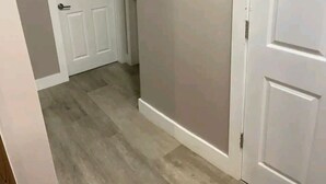 Um corredor com piso de madeira, paredes brancas e uma porta branca no final.