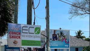 Uma estrada com vários outdoors anunciando negócios locais, incluindo uma loja de conchas e uma empresa de sistemas de janelas ecológicos.