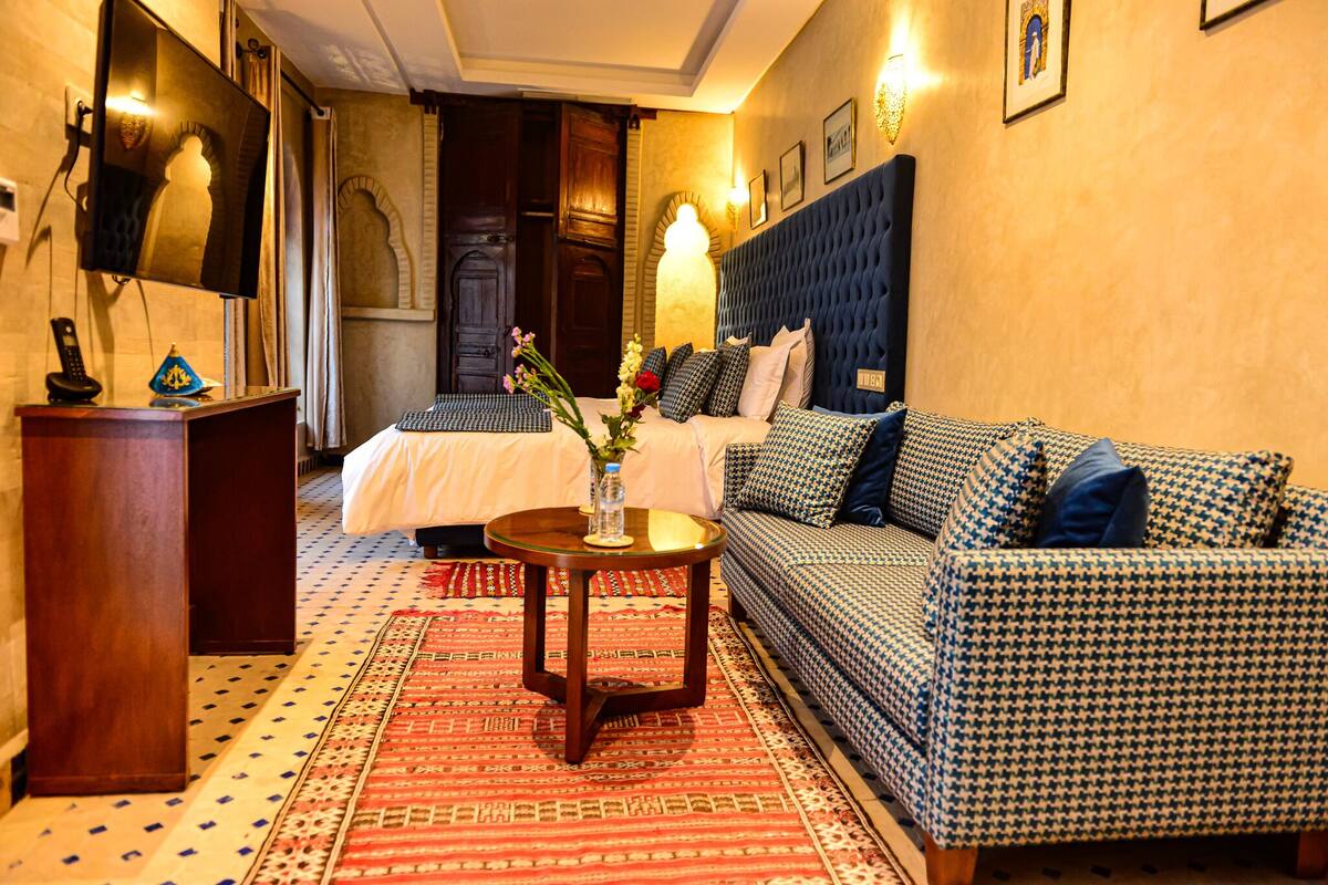 Quarto de hotel com cama, sofá, mesa pequena com um vaso e decoração na parede.