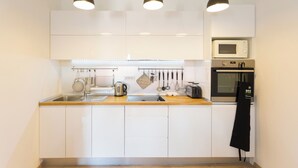 Cozinha moderna com armários brancos, bancada de madeira, pia, chaleira, torradeira, micro-ondas e forno. Três luminárias pendentes sobre a bancada.