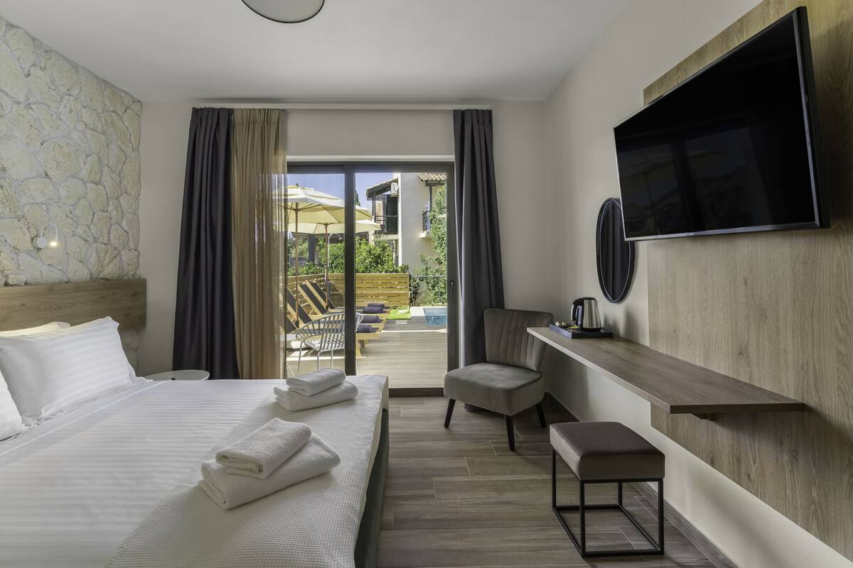 Quarto de hotel com cama, escrivaninha, cadeira, televisão e vista para a área externa.