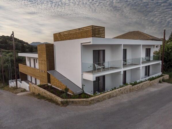Um edifício moderno de dois andares com telhado plano, paredes externas brancas e uma varanda com cadeiras brancas.