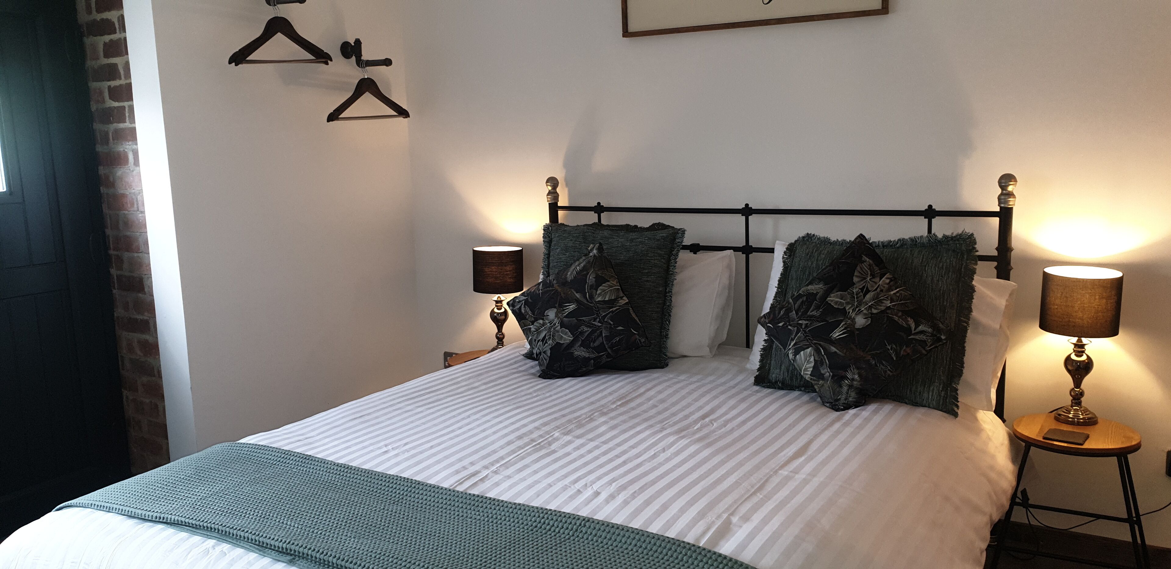 Cama bem arrumada com roupa de cama listrada, duas almofadas decorativas, um cobertor verde e duas luminárias de cabeceira em mesas de cabeceira de madeira.