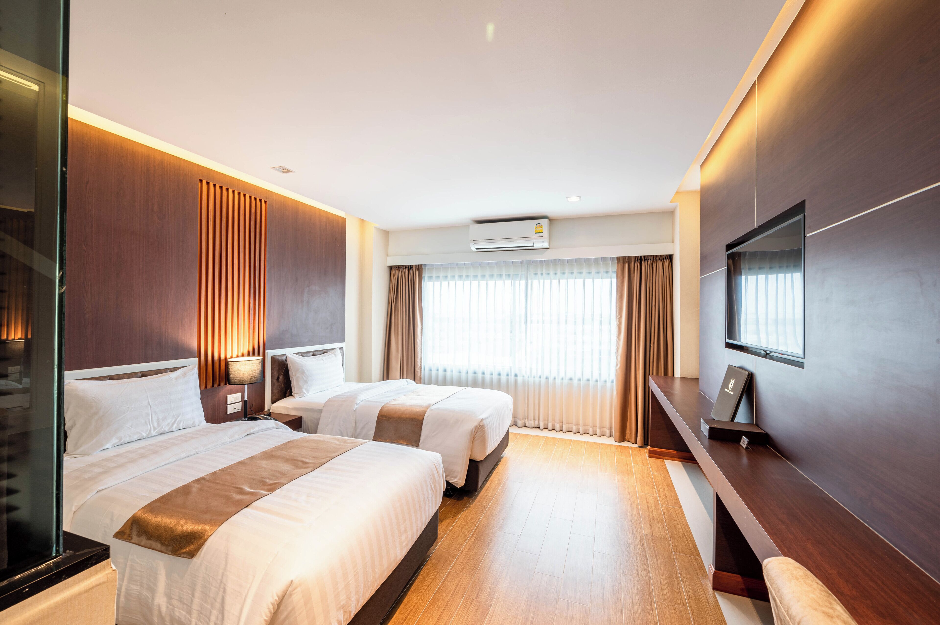 Quarto de hotel com duas camas, uma televisão de tela plana, aparelho de ar condicionado e uma janela grande com cortinas.