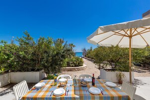 Uma área de refeições ao ar livre com uma mesa posta para dois, com vista para uma praia e um céu azul claro.
