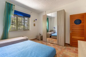 Quarto com duas camas, guarda-roupa, espelho e janela com cortinas.