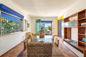 Uma sala de estar ampla com uma longa mesa de madeira, cadeiras de vime e uma estante de livros.