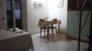 Uma área de refeições com uma mesa posta para quatro pessoas, cadeiras e uma janela com persianas.