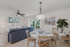 Uma sala de estar moderna com um sofá azul, mesa de jantar com cadeiras e um ventilador de teto.