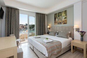 Quarto de hotel com cama, mesas de cabeceira, escrivaninha e vista para o mar.