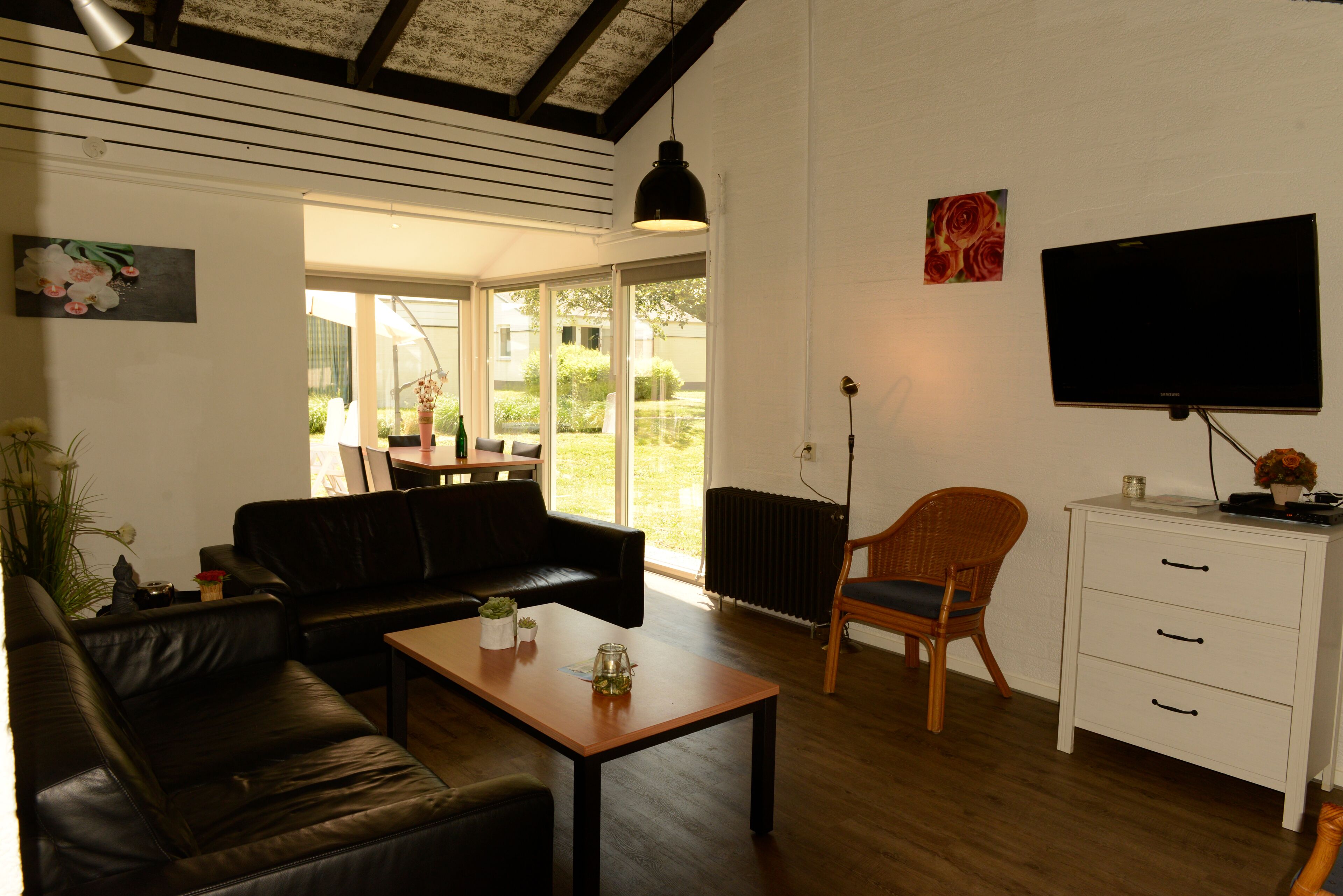 Uma sala de estar com um sofá de couro preto, uma mesa de centro de madeira, um armário branco e uma televisão sobre um suporte.