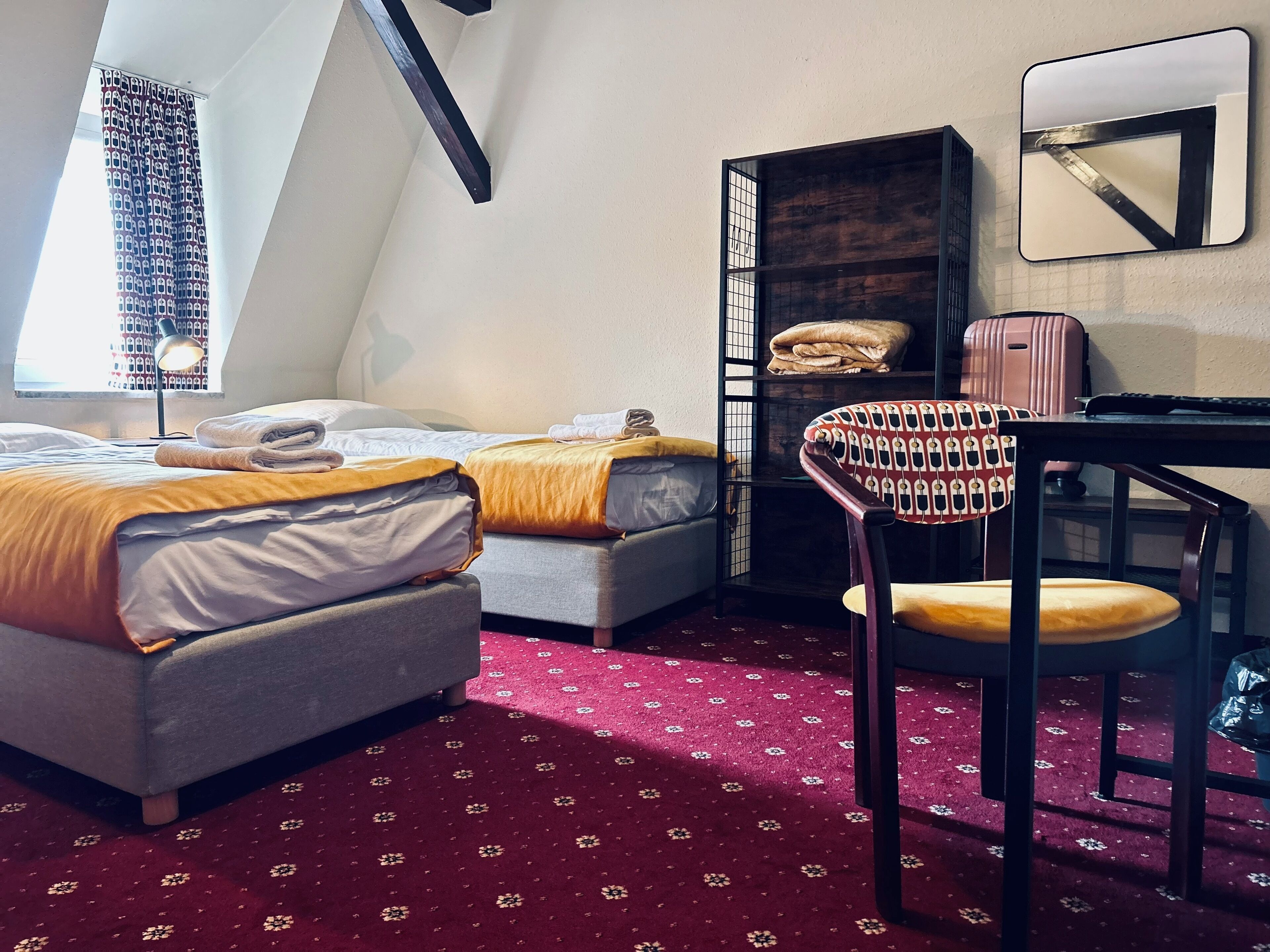 Quarto de hotel com cama, escrivaninha, cadeira, guarda-roupa e janela com cortinas.