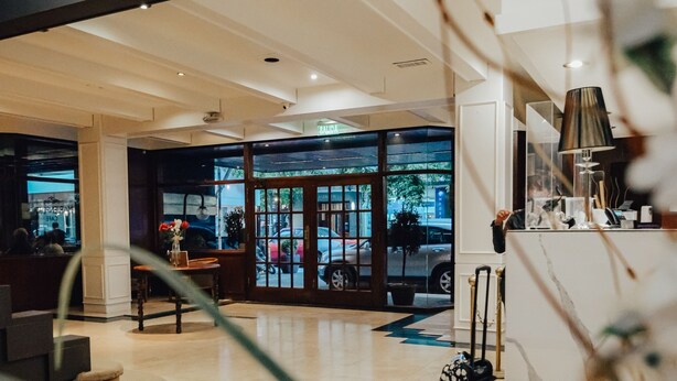 Um saguão de hotel com balcão de recepção, área de estar e vista para a rua.