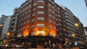 Um hotel de vários andares com entrada de canto, várias varandas e um restaurante no térreo.