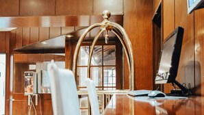 Um saguão de hotel com balcão de atendimento em madeira, um monitor de computador e uma área de estar com cadeiras.