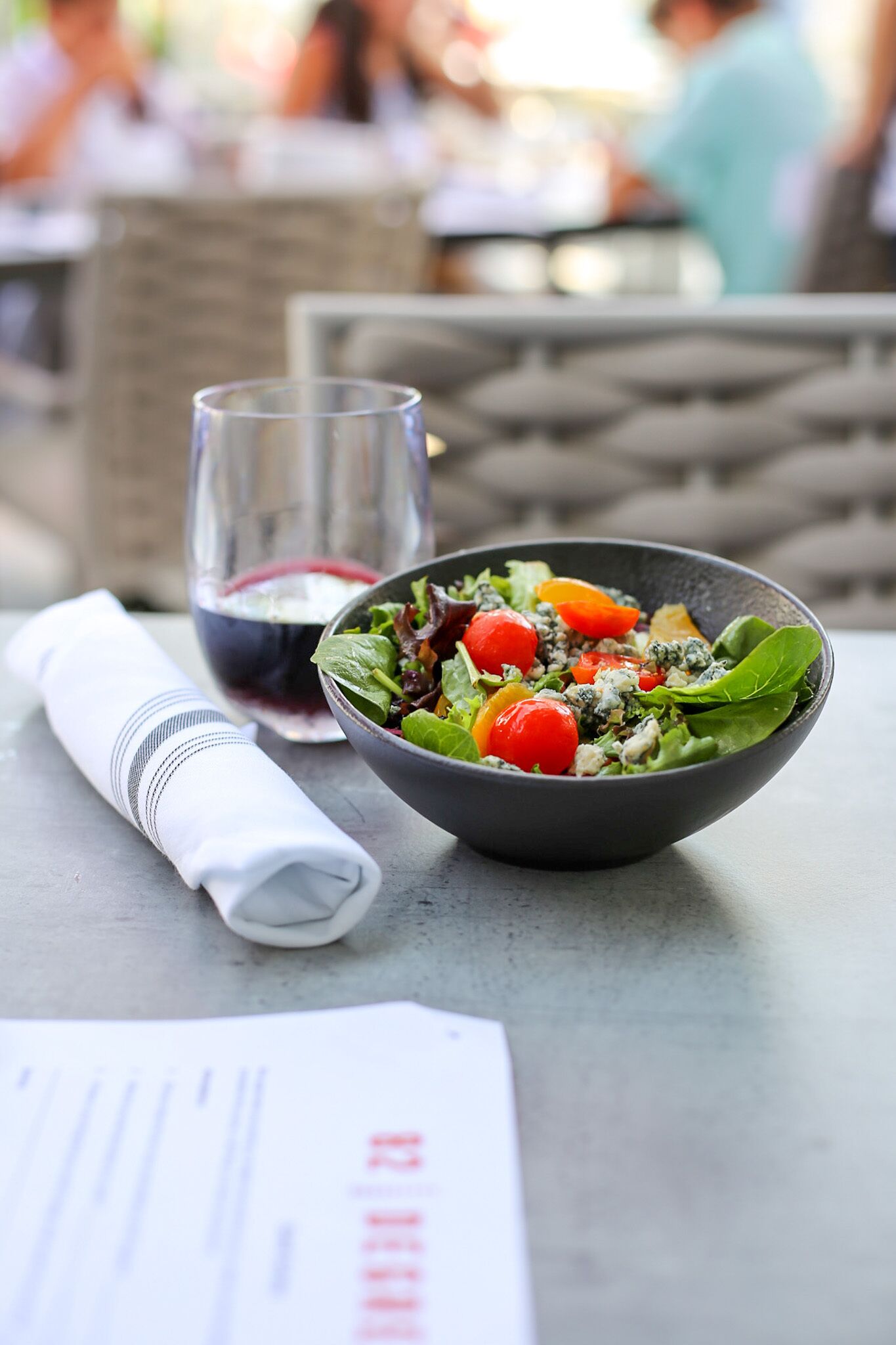 Uma salada numa tigela com um copo de vinho tinto sobre uma mesa.