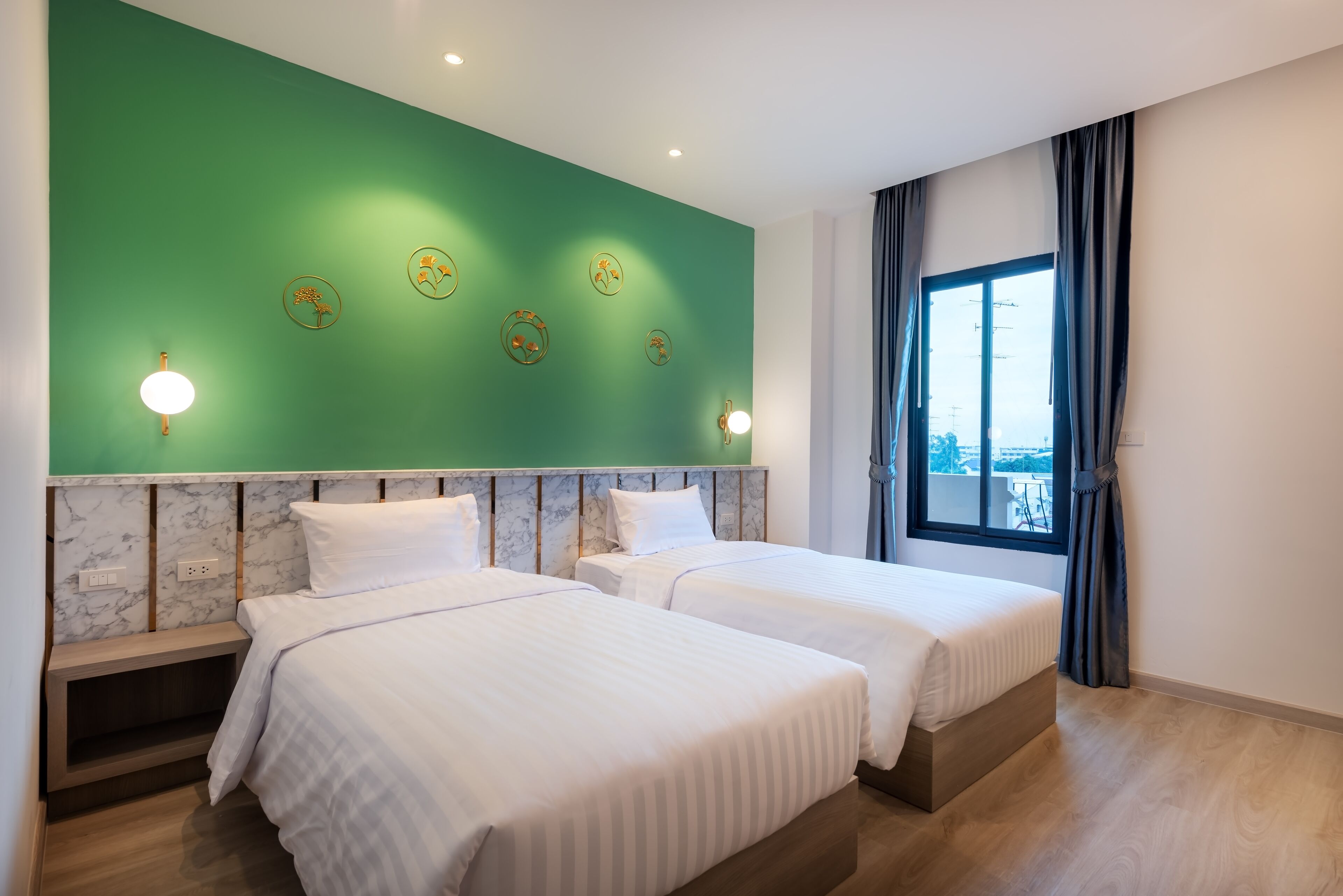 Quarto de hotel com duas camas, uma parede de destaque verde e uma janela com cortinas.