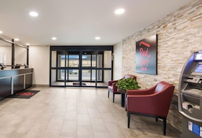 Uma área de recepção com design moderno, incluindo um balcão de atendimento, espaço de espera com cadeiras, um vaso de planta e uma placa na parede.