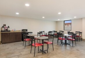 Sala de conferências com mesas, cadeiras, cozinha compacta e tela de projeção na parede.