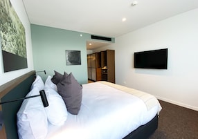 Quarto de hotel com uma cama, uma televisão de tela plana na parede e um quadro na parede.
