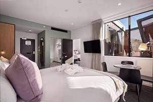 Quarto de hotel com cama, escrivaninha, cadeira, televisão e janela com vista para o exterior.