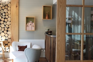 Um quarto aconchegante com sofá branco, cadeira cinza, painéis de parede de madeira e um armário de vidro com objetos em cima.