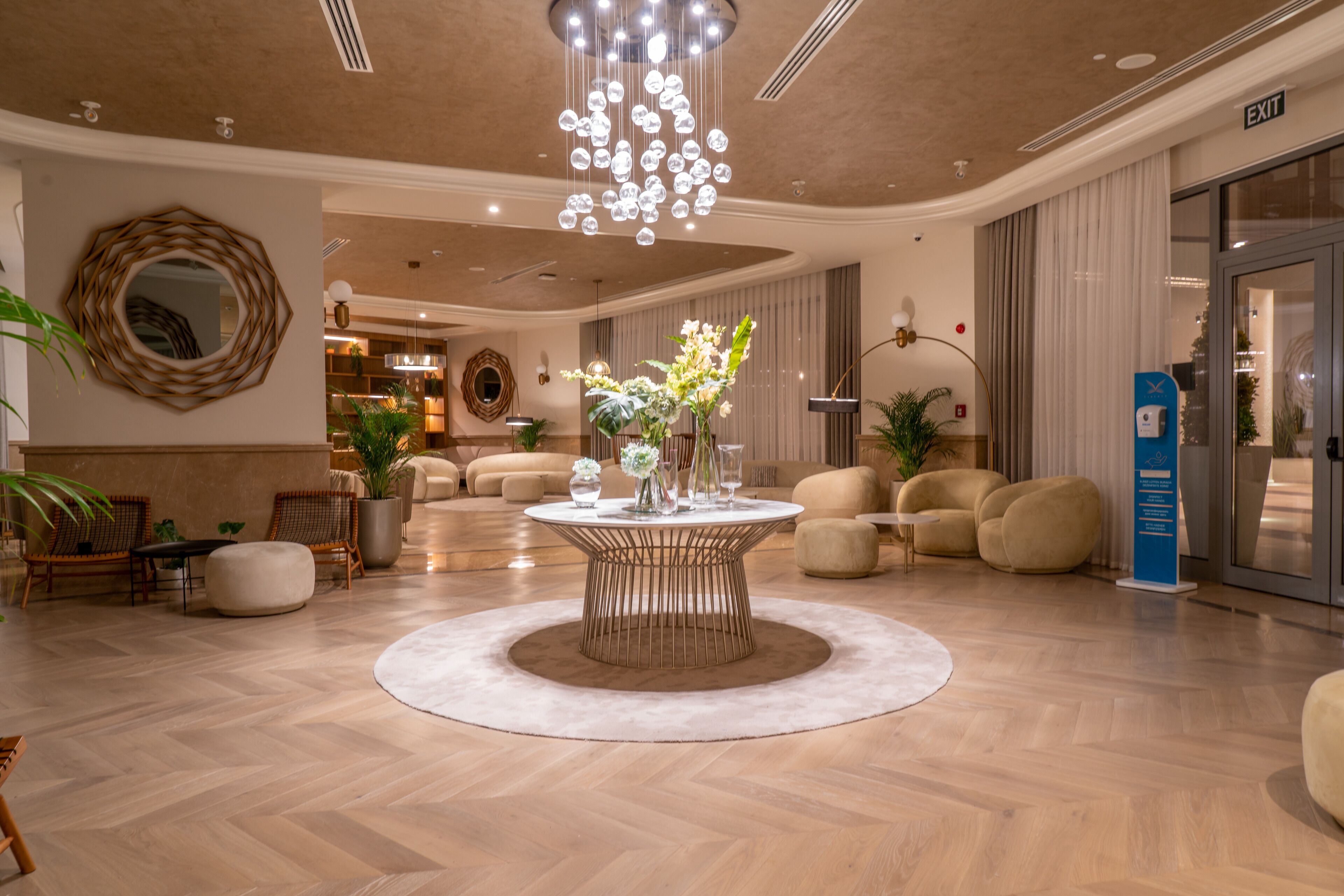 Um hall amplo com uma mesa redonda central, assentos confortáveis e um lustre moderno.