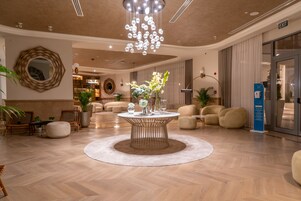 Um hall amplo com uma mesa redonda central, assentos confortáveis e um lustre moderno.