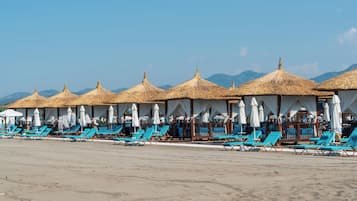 Uma praia com fileiras de guarda-sóis de palha e cadeiras de banho azuis.