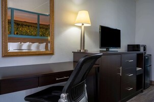 Quarto de hotel com uma cama, uma mesa com luminária, televisão, micro-ondas e frigorífico.
