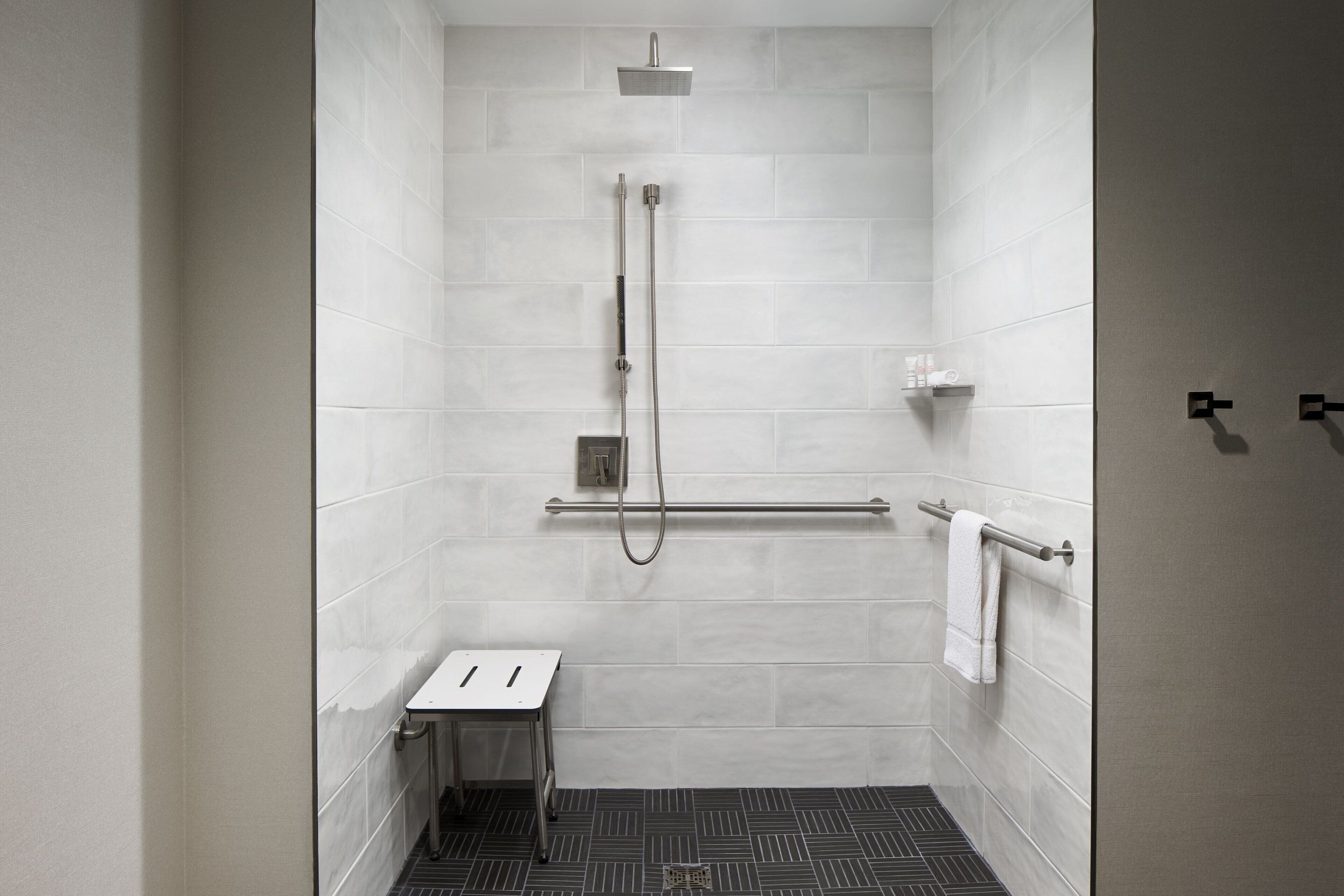 Uma casa de banho moderna com azulejos brancos, chuveiro, porta-toalhas e uma pequena mesa.