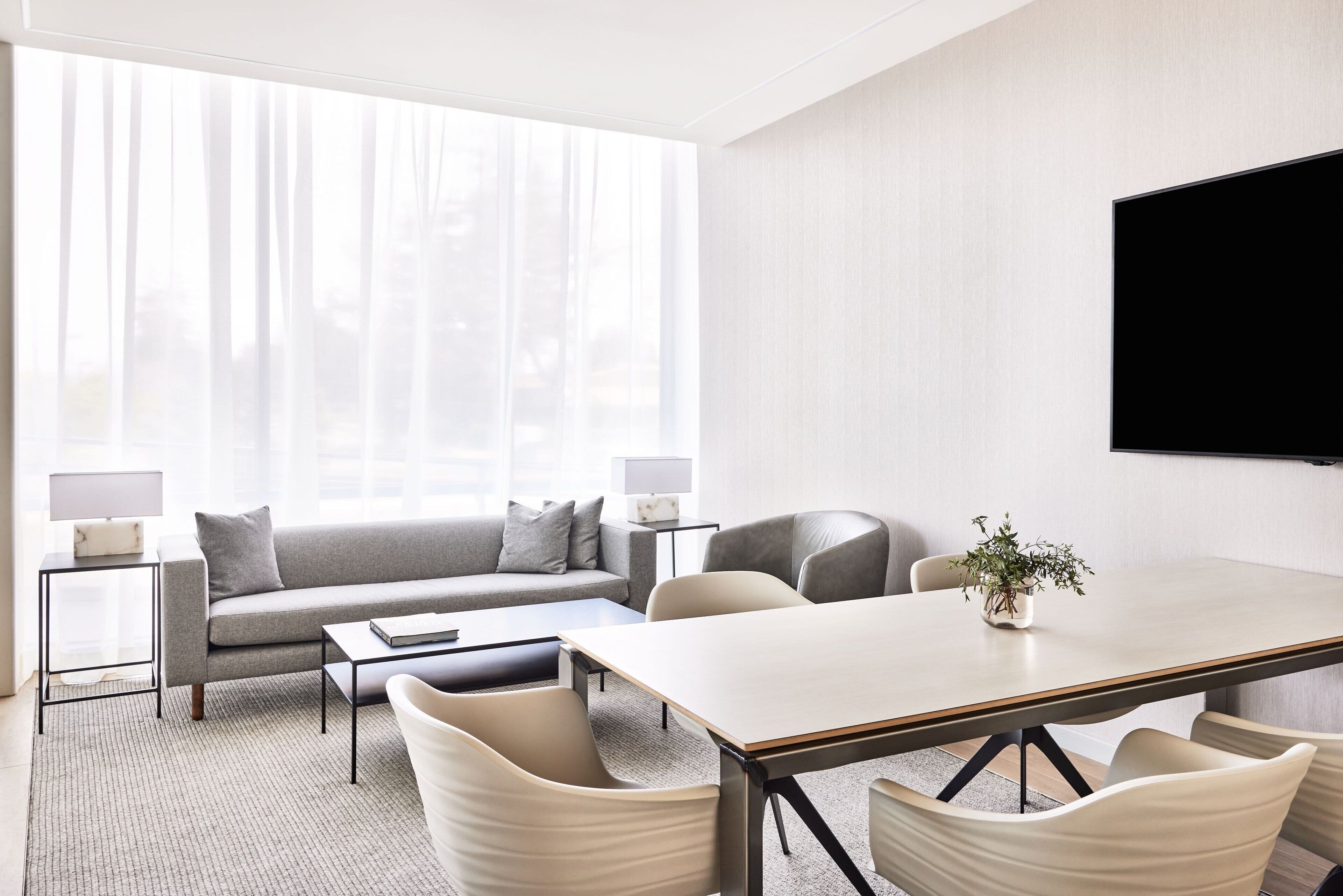 Quarto de hotel moderno com sofá, mesa de jantar e TV fixada na parede.