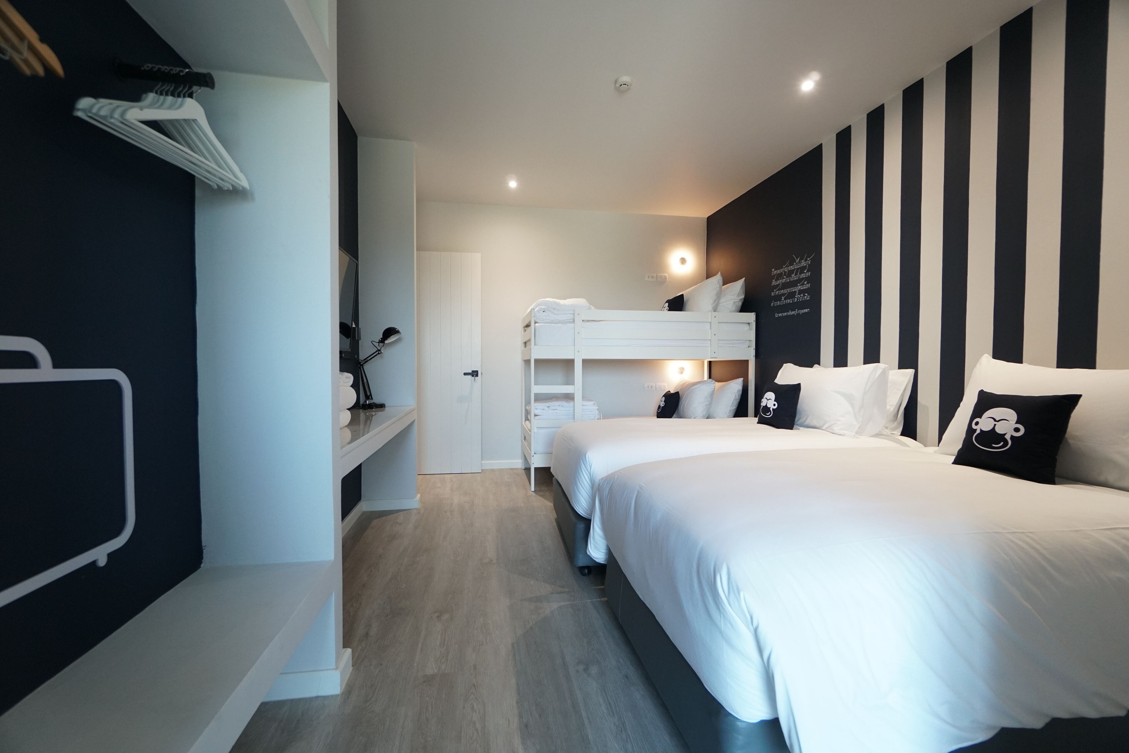 Quarto de hotel moderno com beliche, guarda-roupa branco e parede listrada.