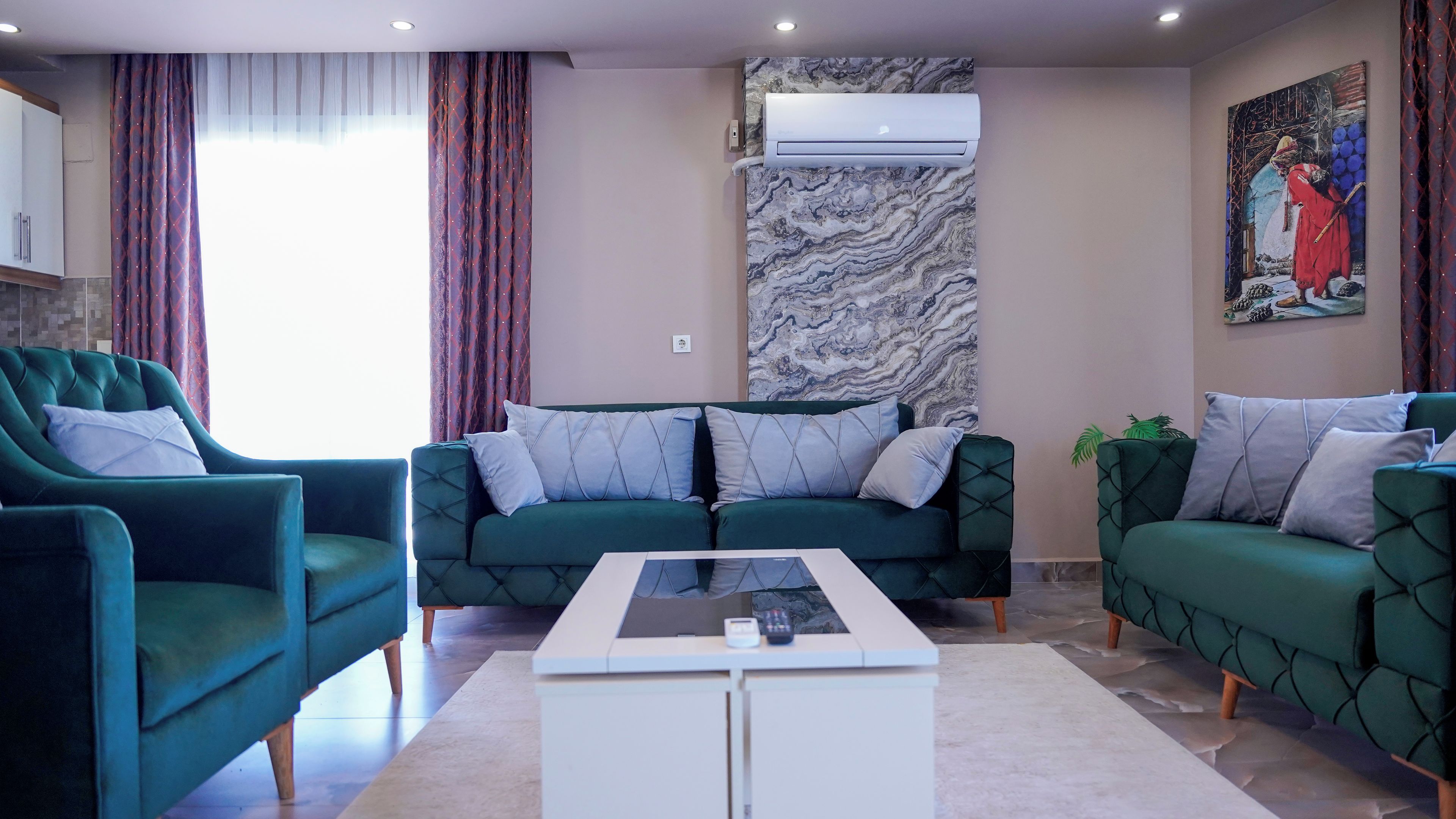 Sala de estar com sofá verde, mesa de centro branca e parede com padrão marmorizado.