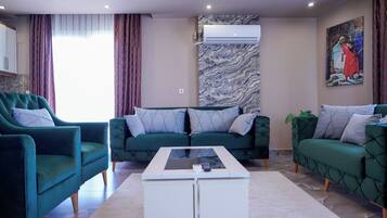 Sala de estar com sofá verde, mesa de centro branca e parede com padrão marmorizado.