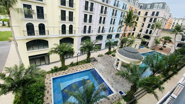 Um hotel com vários andares, varandas, piscina e palmeiras.