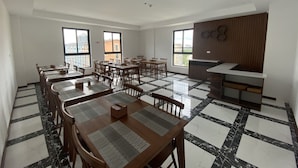 Uma sala de jantar espaçosa com várias mesas e cadeiras, amplas janelas com vista e uma cozinha moderna.
