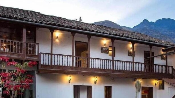 Um edifício tradicional com varanda, várias janelas e montanhas ao fundo.