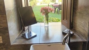 Uma casa de banho com uma pia grande, uma pequena mesa com um computador portátil e um vaso com flores.
