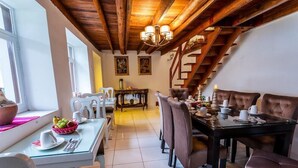 Uma sala de jantar com teto de madeira, um candelabro e uma escadaria que leva a um andar superior.