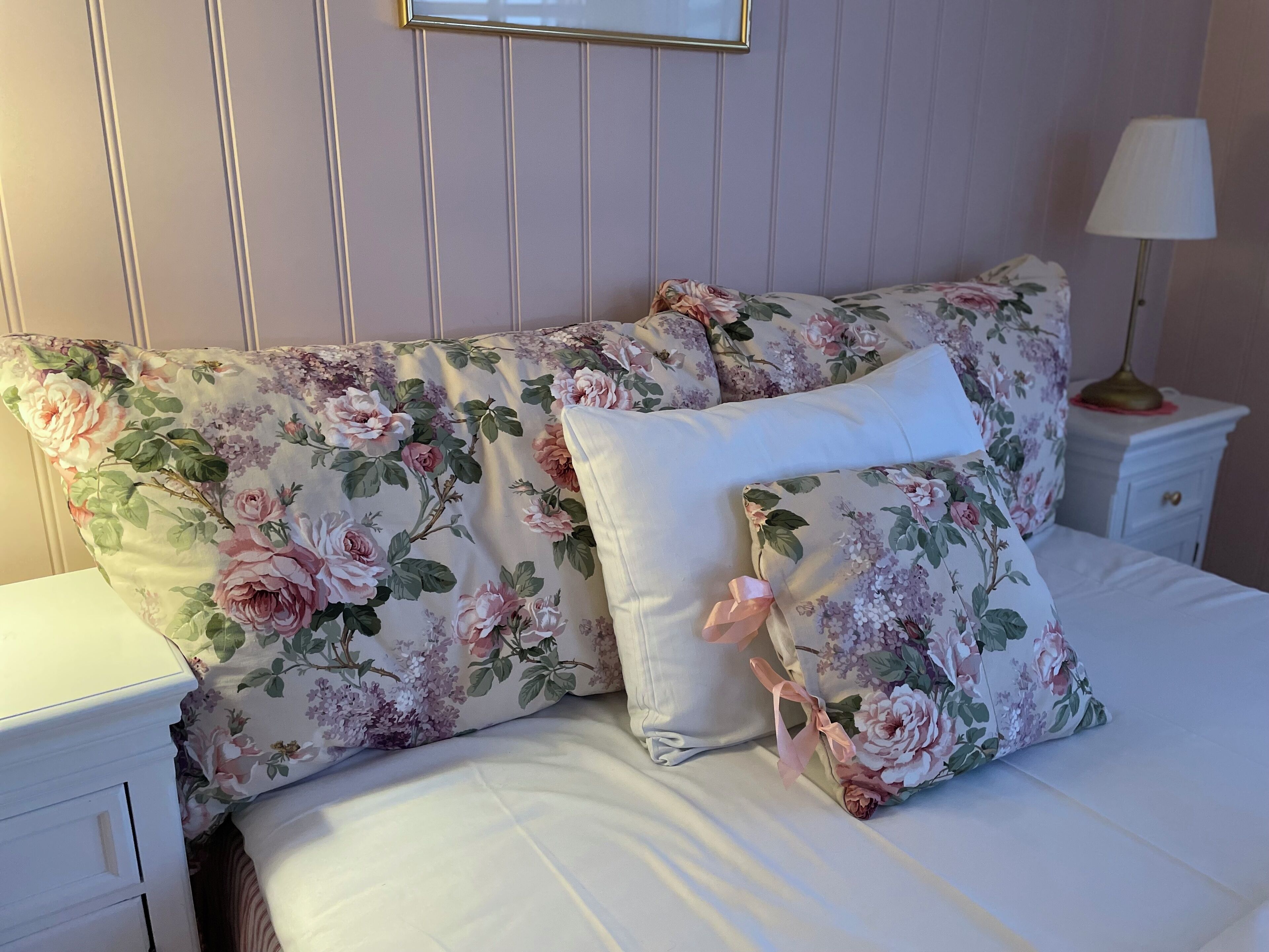 Uma cama com roupa de cama estampada com flores e uma mesa de cabeceira com abajur.