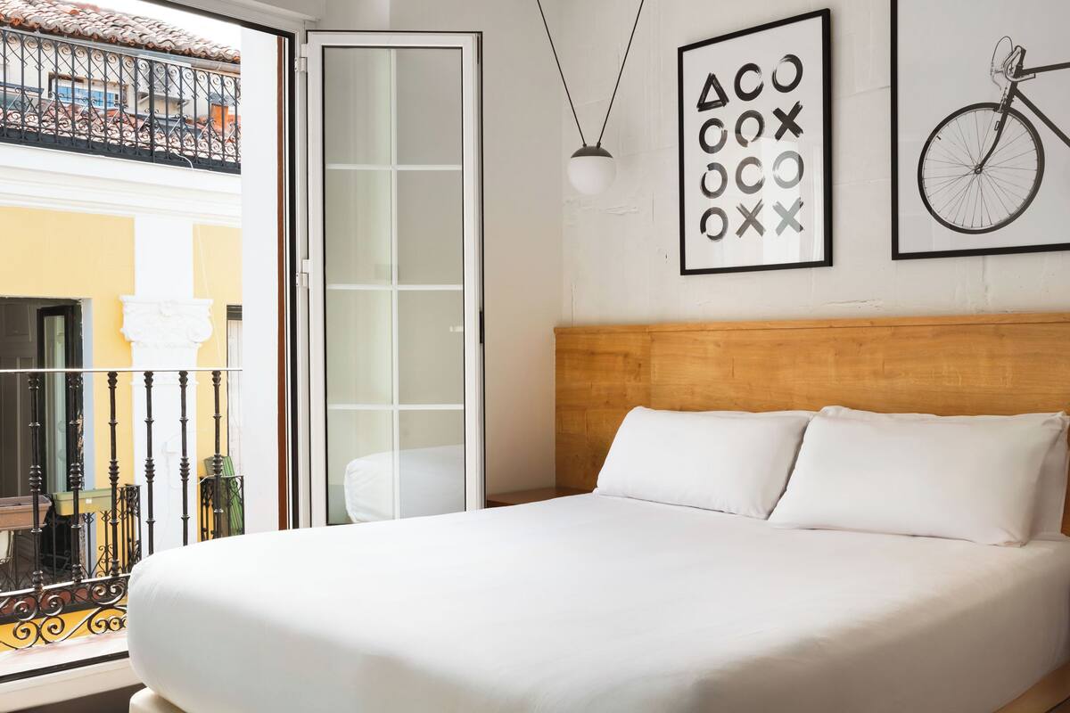 Quarto com cabeceira de madeira, roupa de cama branca e duas imagens emolduradas na parede.