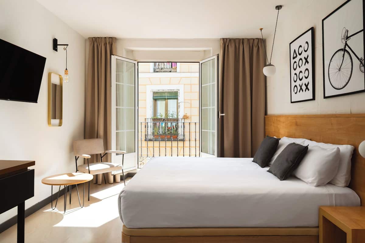 Quarto de hotel com cama, mesas de cabeceira, escrivaninha, televisão e varanda com plantas.