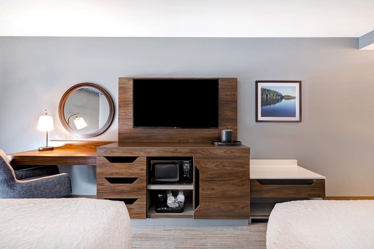 Quarto de hotel com escrivaninha de madeira, televisão de tela plana, espelho, quadro emoldurado e uma cama.